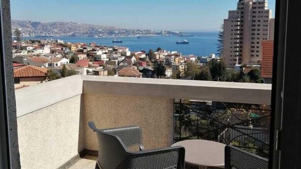 Varanda com duas cadeiras e uma mesa, vista para um horizonte costeiro com edifícios e o mar.