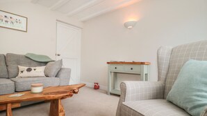 Uma sala de estar acolhedora com um sofá cinza, uma mesa de centro de madeira, uma poltrona xadrez, uma escrivaninha pequena e um luminário fixado na parede.