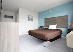 Quarto de hotel moderno com cama, mesa de cabeceira e pequena escrivaninha com cadeira.