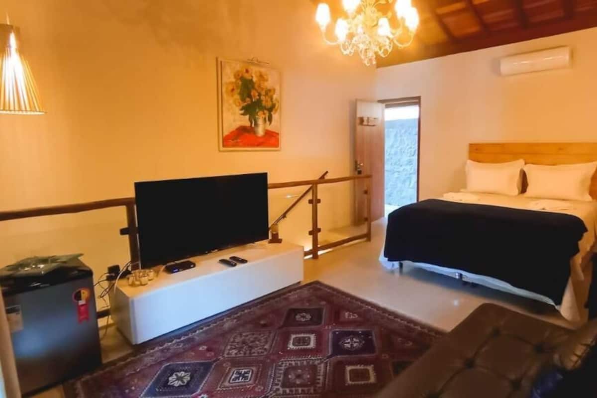 Quarto com cama, televisão, escrivaninha e cadeira.