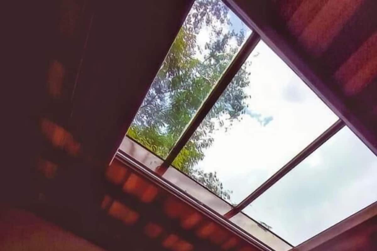 Um quarto com claraboia, cama com roupa de cama branca, porta de madeira e uma TV sobre um suporte de madeira.
