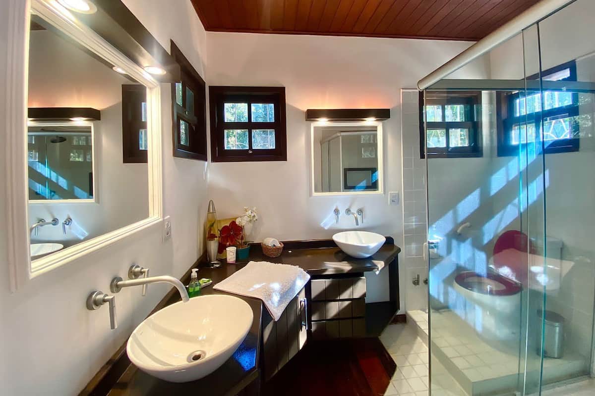 Uma casa de banho moderna com uma grande pia, dois espelhos e cabine de duche em vidro.