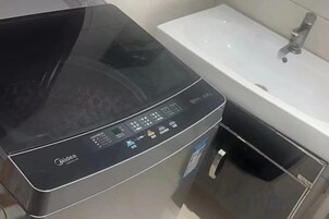 Um eletrodoméstico preto com visor digital, pia e torneira em um banheiro.
