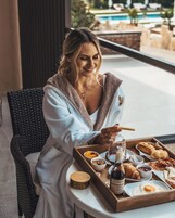 Uma pessoa sentada à mesa com uma bandeja de itens de café da manhã, incluindo pão, ovos e doces.