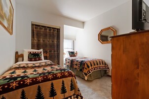 Quarto com duas camas, cômoda de madeira, espelho e janela com persianas.