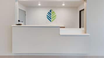 Uma área de recepção com um balcão branco, um logotipo verde e azul na parede e uma porta à esquerda.