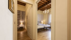Um corredor leva a um quarto com chão de madeira, parede de pedra e um candelabro.