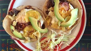 Dois tacos com abacate e bacon num prato com borda vermelha.