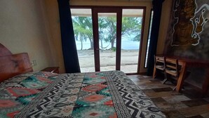 Quarto com cama, escrivaninha e vista para a praia através de uma porta de correr.