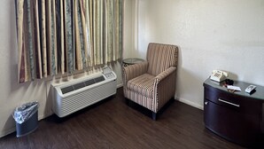 Quarto com radiador, poltrona listrada, mesa pequena, telefone e lixeira.