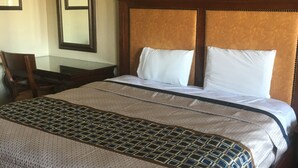 Quarto de hotel com uma cama grande, cabeceira de madeira, escrivaninha com cadeira e duas molduras na parede.