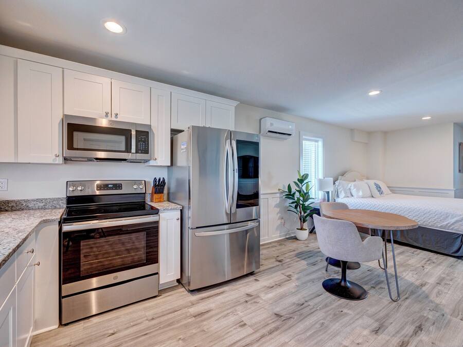 Cozinha moderna com eletrodomésticos de aço inoxidável, uma área de refeições com mesa e cadeiras, e uma cama no quarto adjacente.