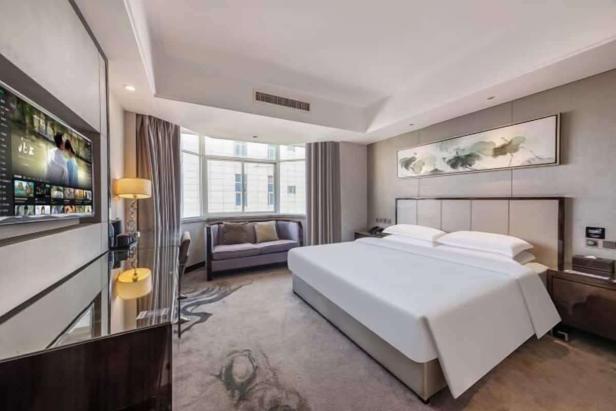 Quarto de hotel com uma cama grande, um sofá, uma televisão e um quadro na parede.