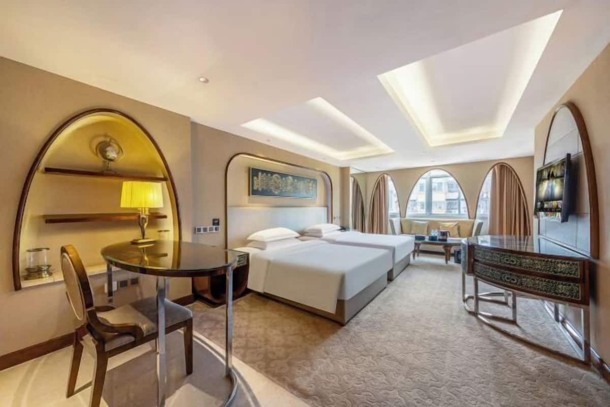 Quarto de hotel com cama, escrivaninha, cadeira, televisão e janela.