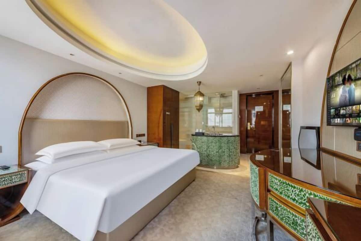 Quarto de hotel com cama, toucador com espelho, banheiro pequeno e televisão.