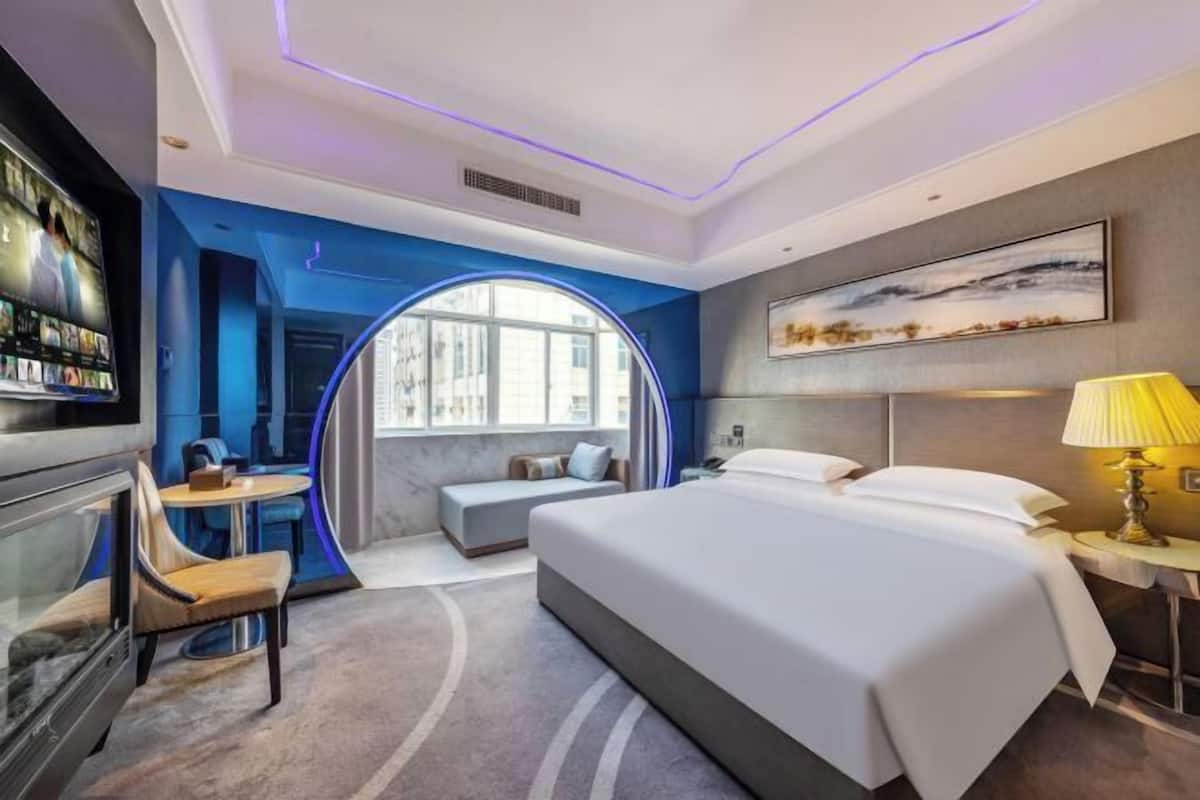 Quarto de hotel moderno com uma cama grande, uma mesa de escritório, área de estar e televisão.