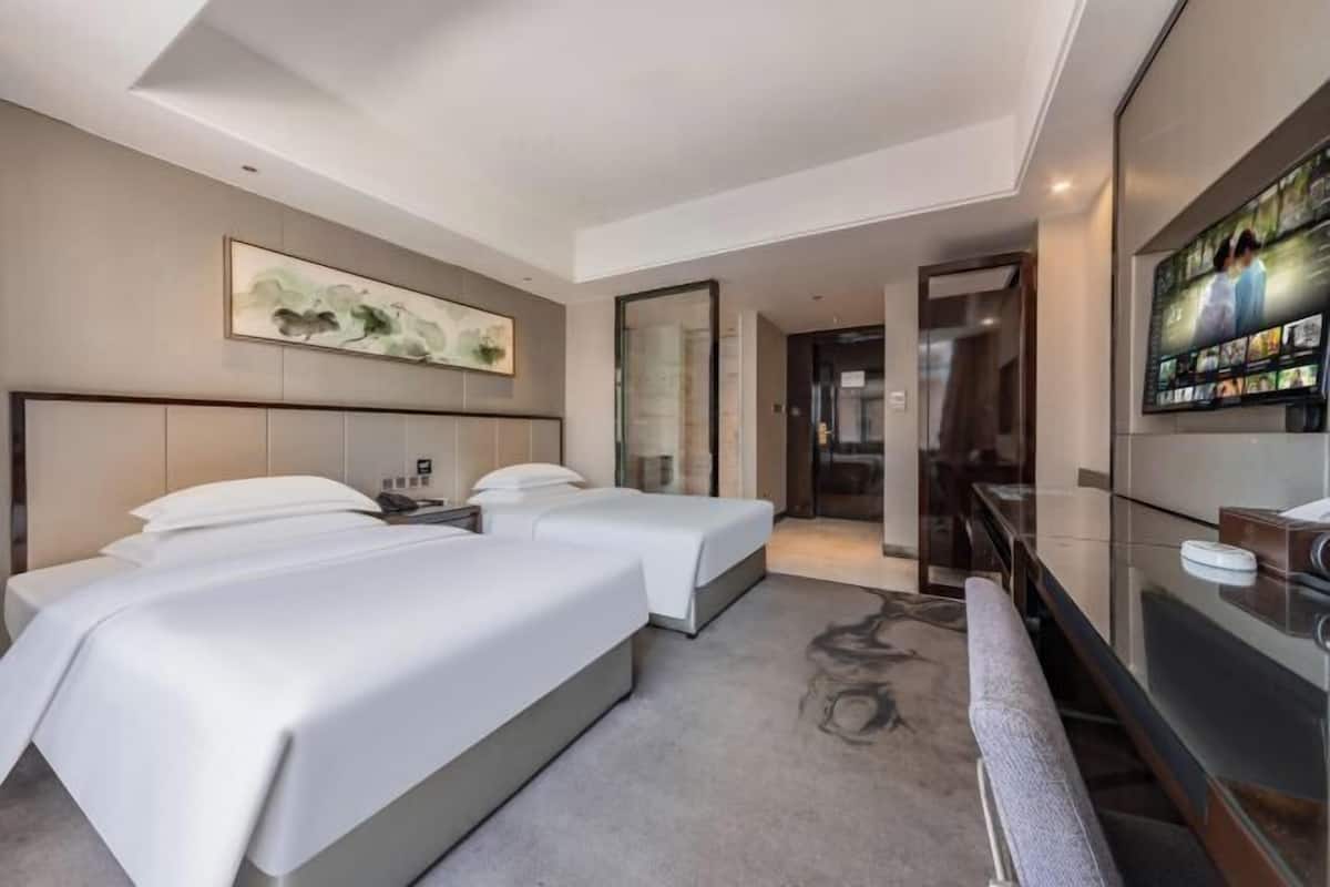 Quarto de hotel com duas camas, um espelho grande, uma televisão e um quadro na parede.