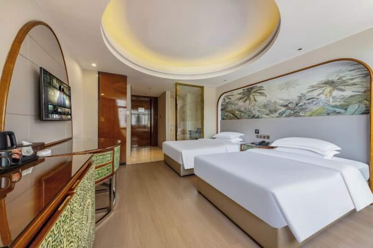 Quarto de hotel com duas camas, televisão, escrivaninha e uma grande pintura na parede.