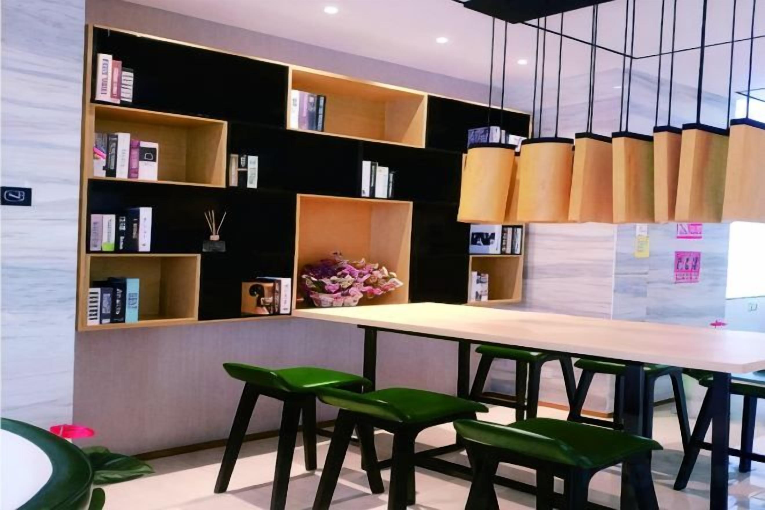 Um interior moderno com uma mesa comprida e cadeiras verdes, rodeado por estantes pretas com livros e objetos decorativos.