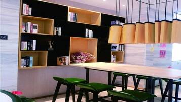 Um interior moderno com uma mesa comprida e cadeiras verdes, rodeado por estantes pretas com livros e objetos decorativos.