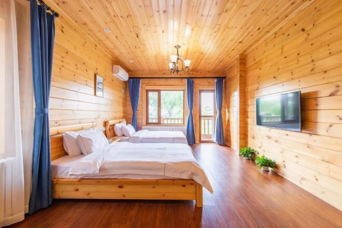 Quarto de cabana de madeira com duas camas, uma TV e janela com cortinas.