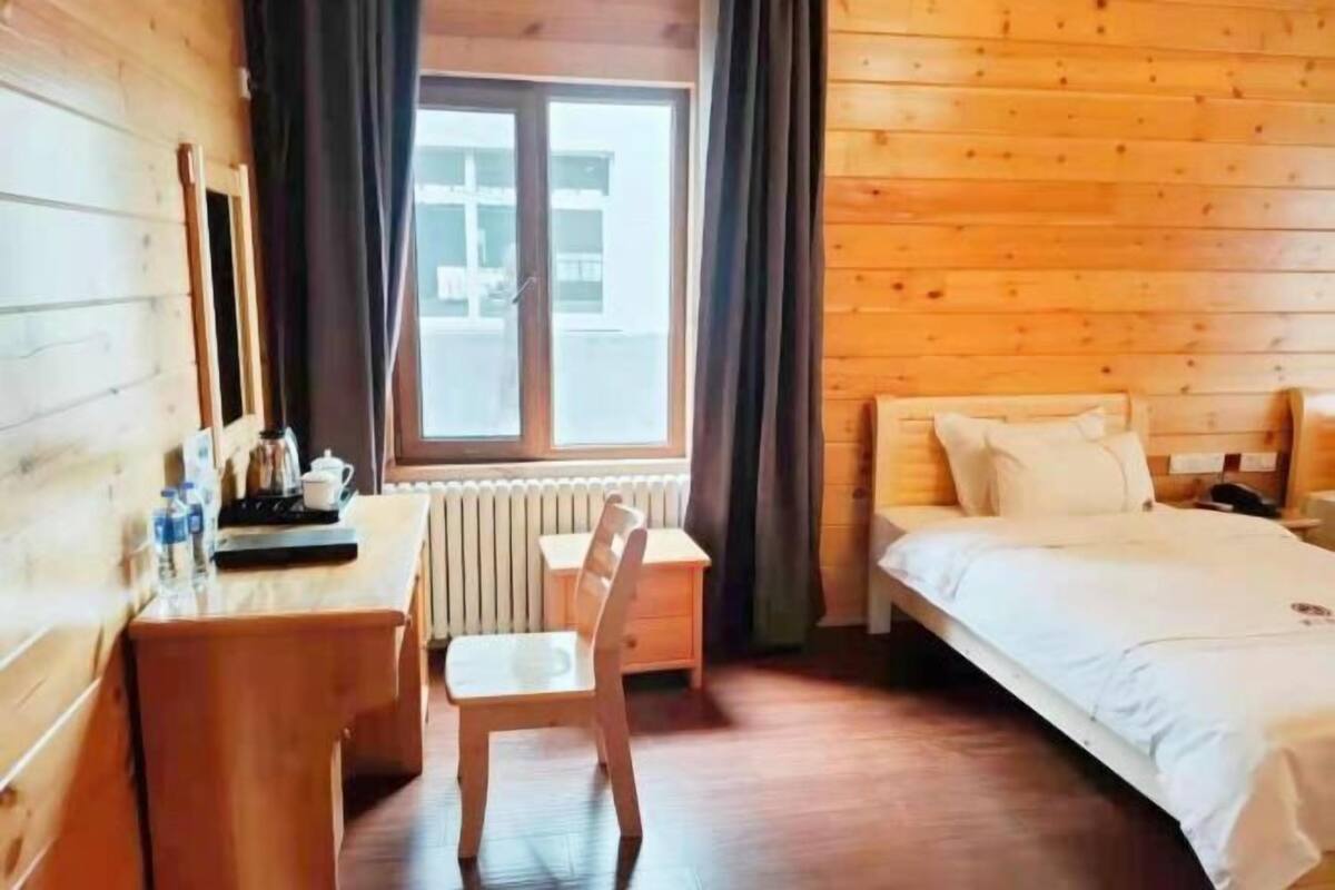 Quarto de madeira com uma cama, uma escrivaninha e uma cadeira.