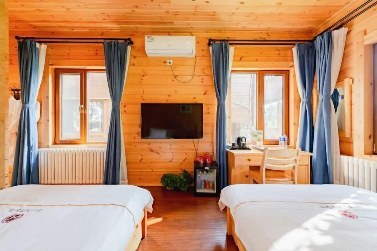 Quarto de cabana de madeira com duas camas, uma TV, uma escrivaninha e uma cadeira.