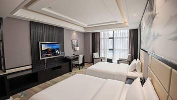 Quarto de hotel com duas camas, uma escrivaninha, uma televisão e uma janela grande.