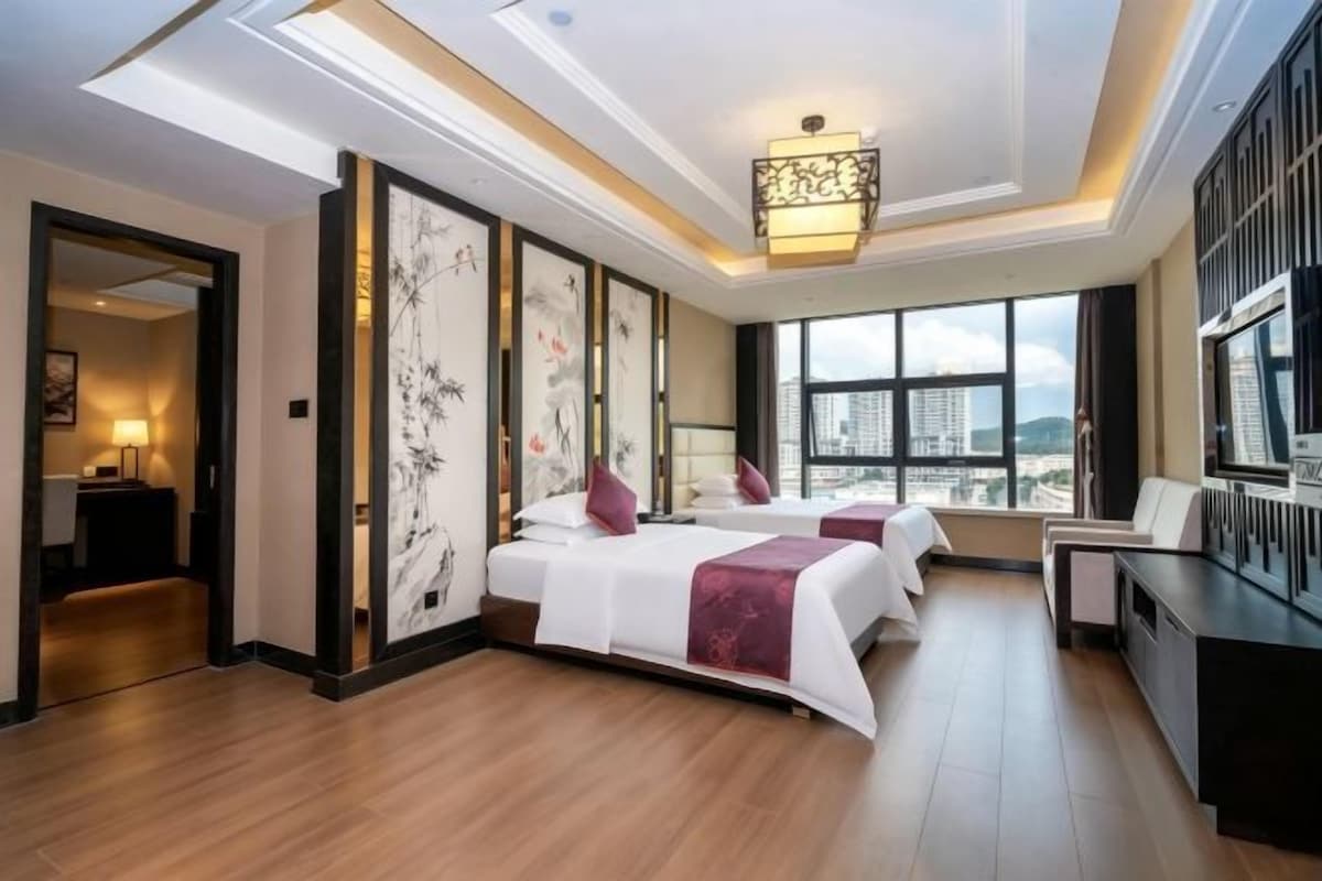 Quarto de hotel com duas camas, uma escrivaninha e uma janela grande com vista para a cidade.