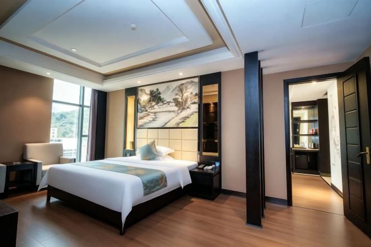 Quarto de hotel moderno com uma cama grande, mesas de cabeceira e uma janela ampla.