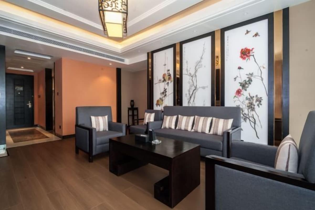 Uma sala de estar moderna com um sofá, poltronas e uma mesa de centro. Há painéis decorativos na parede e uma porta ao fundo.