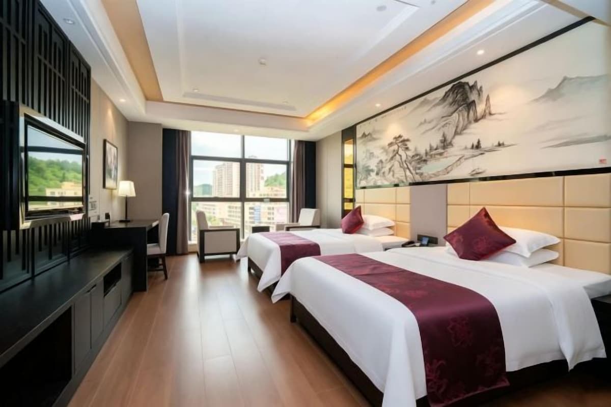 Quarto de hotel com duas camas, uma escrivaninha e uma janela grande.
