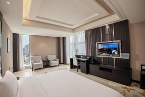 Quarto de hotel com uma cama grande, uma escrivaninha com cadeira, televisão e vista para a cidade.