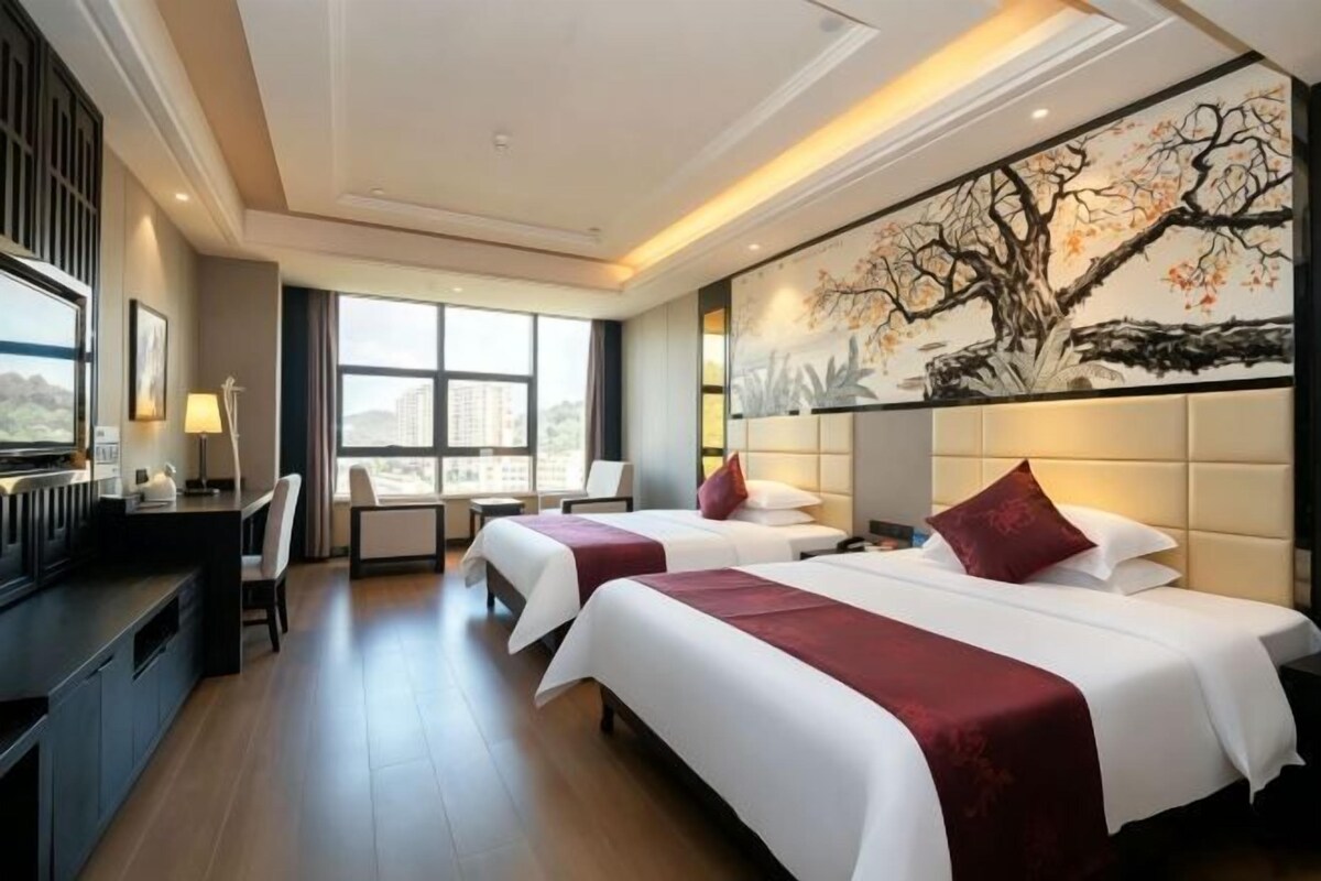 Quarto de hotel com duas camas, uma escrivaninha, uma cadeira e uma janela grande.