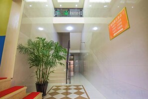 Um saguão de hotel com escadas, uma planta em vaso e um chão quadriculado.