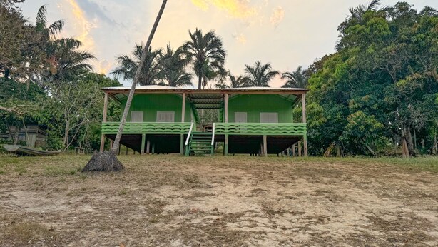 Um edifício verde de dois andares com varanda coberta e escadaria que leva ao nível superior.