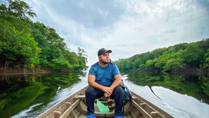 Uma pessoa sentada em um barco de madeira em um rio calmo, cercada por vegetação exuberante.