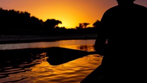 Silhueta de alguém remando um barco ao pôr do sol.