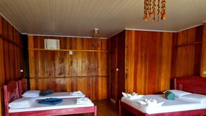 Quarto com duas camas de madeira, cada uma com cabeceira vermelha, roupa de cama branca e toalhas. Teto de madeira com luminária pendente.
