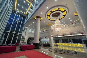 Um hall amplo com um lustre imponente, assentos vermelhos e uma roda decorativa central.
