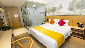Quarto de hotel com uma cama, uma escrivaninha, uma cadeira, um aparelho de café e um box de chuveiro de vidro.