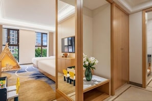 Quarto de hotel com cama, televisão, guarda-roupa, espelho e área de recreação com uma tenda.