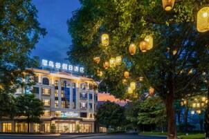 Um hotel com fachada clássica, letreiros iluminados e uma rua arborizada.