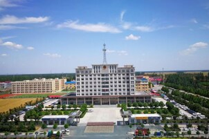 Edifício com vários andares e um pátio central, rodeado por estacionamento e áreas verdes.