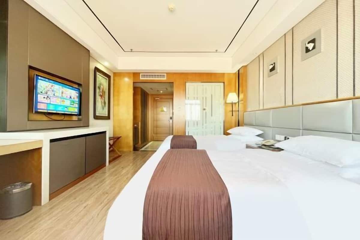 Quarto de hotel com uma cama grande, televisão na parede, escrivaninha e lixeira.