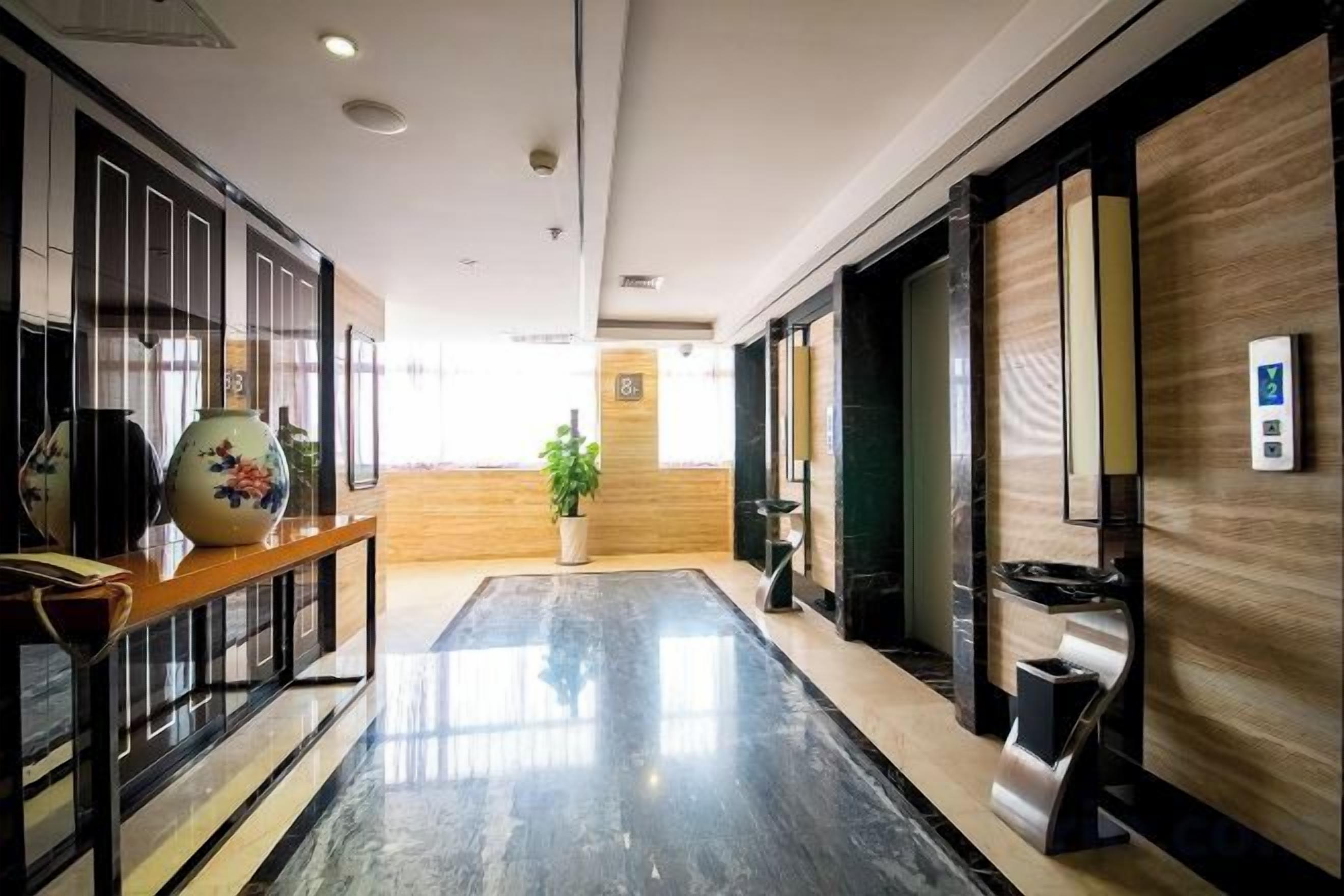 Um hall de hotel com piso lustroso, balcão de recepção, planta em vaso e quadro de avisos fixado na parede.