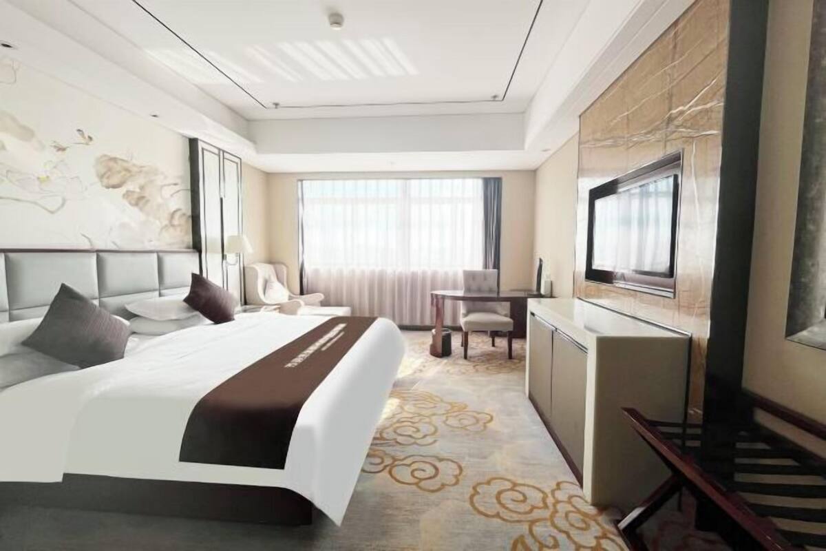 Quarto de hotel moderno com uma cama grande, uma escrivaninha, uma televisão e uma janela com cortinas.