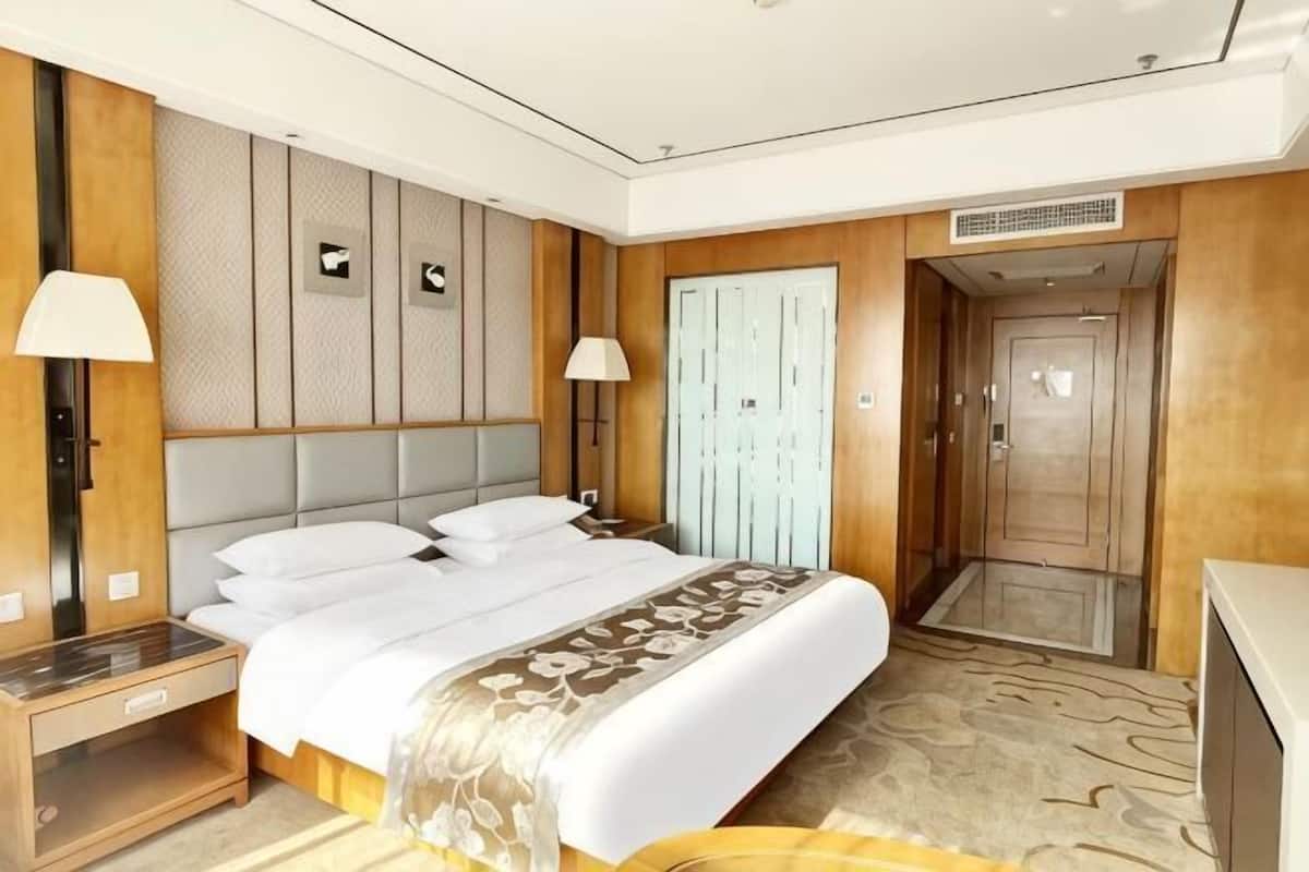 Quarto de hotel com uma cama grande, duas mesas de cabeceira, um guarda-roupa e uma escrivaninha.