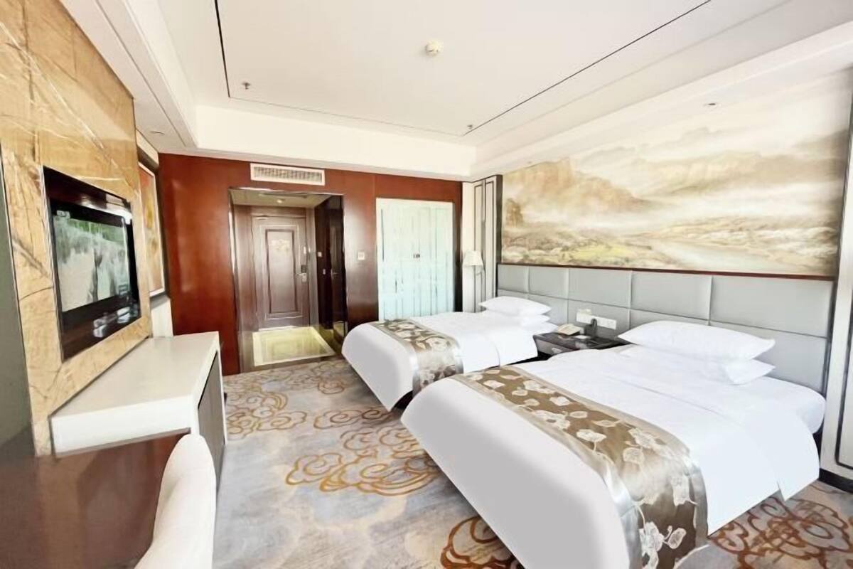 Quarto de hotel com duas camas, televisão de tela plana, escrivaninha e um quadro grande na parede.