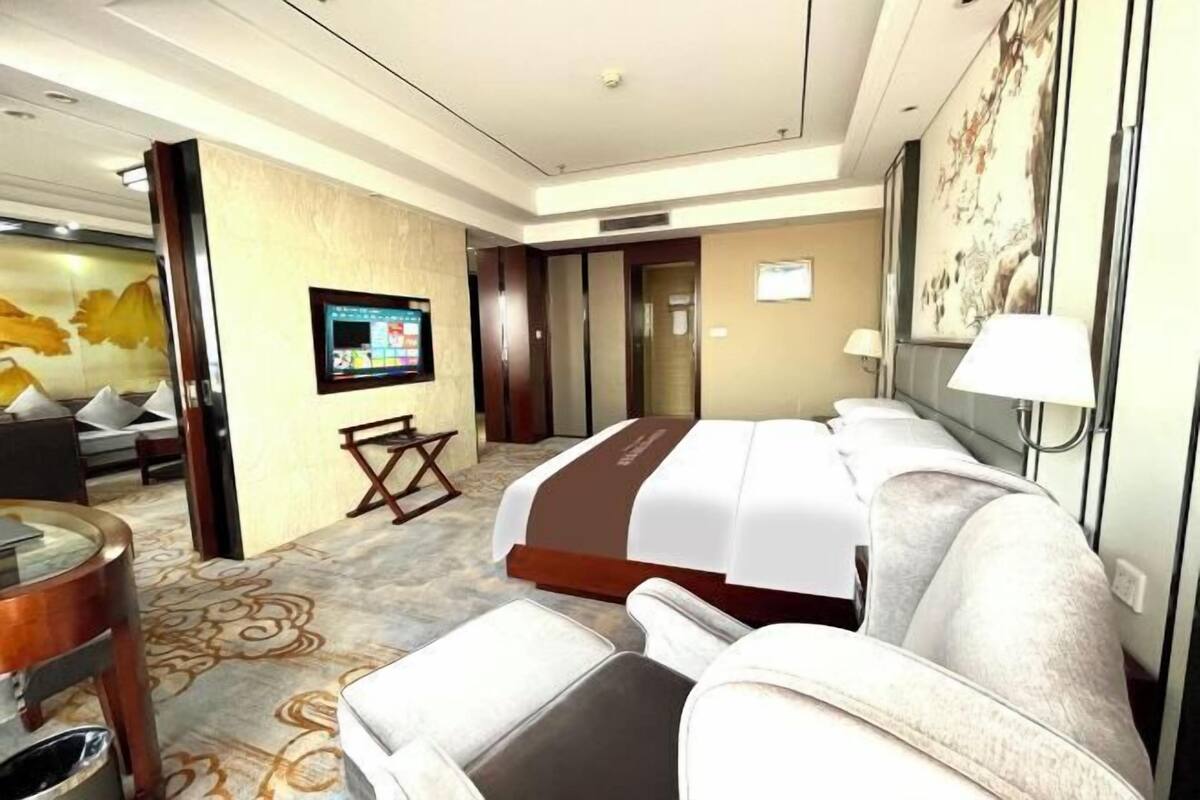 Quarto de hotel com uma cama, escrivaninha, cadeira, televisão e um quadro na parede.
